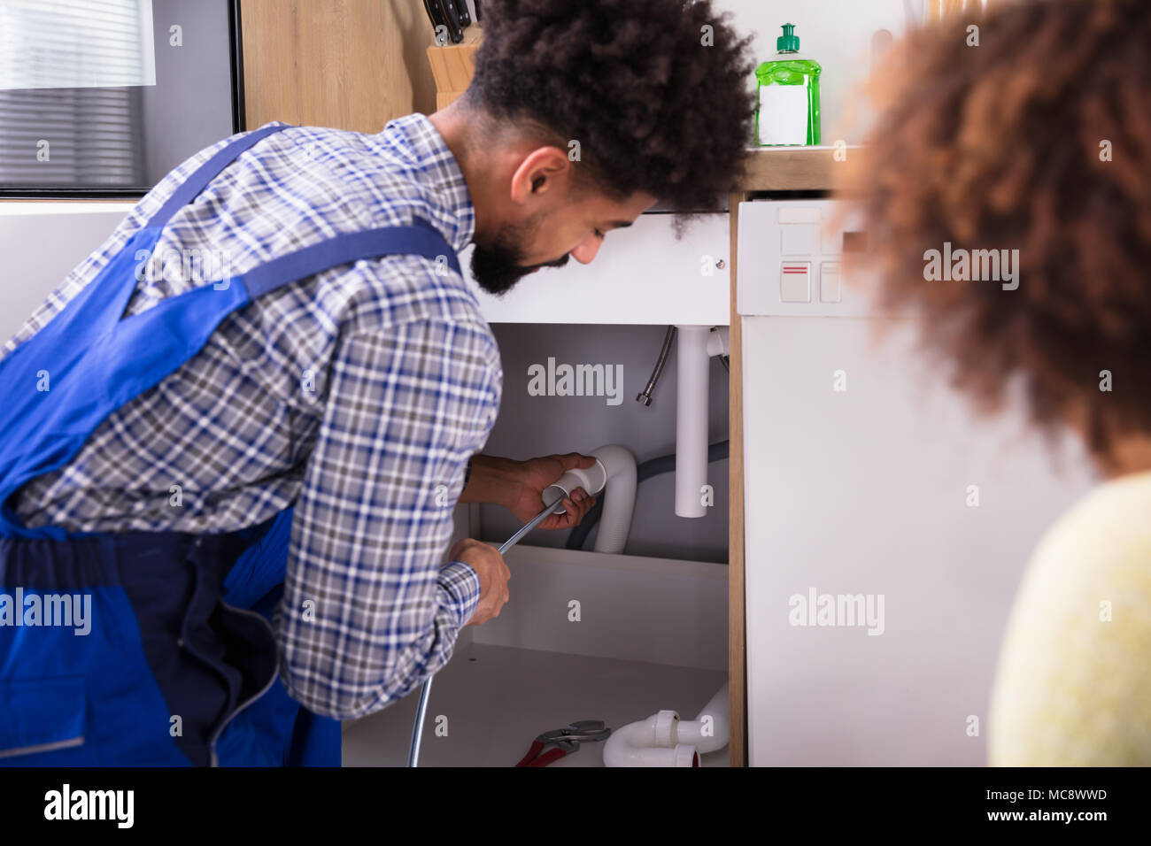 Woman Looking At Male Plumber Cleaning Clogged Pipes Stock Photo - Alamy