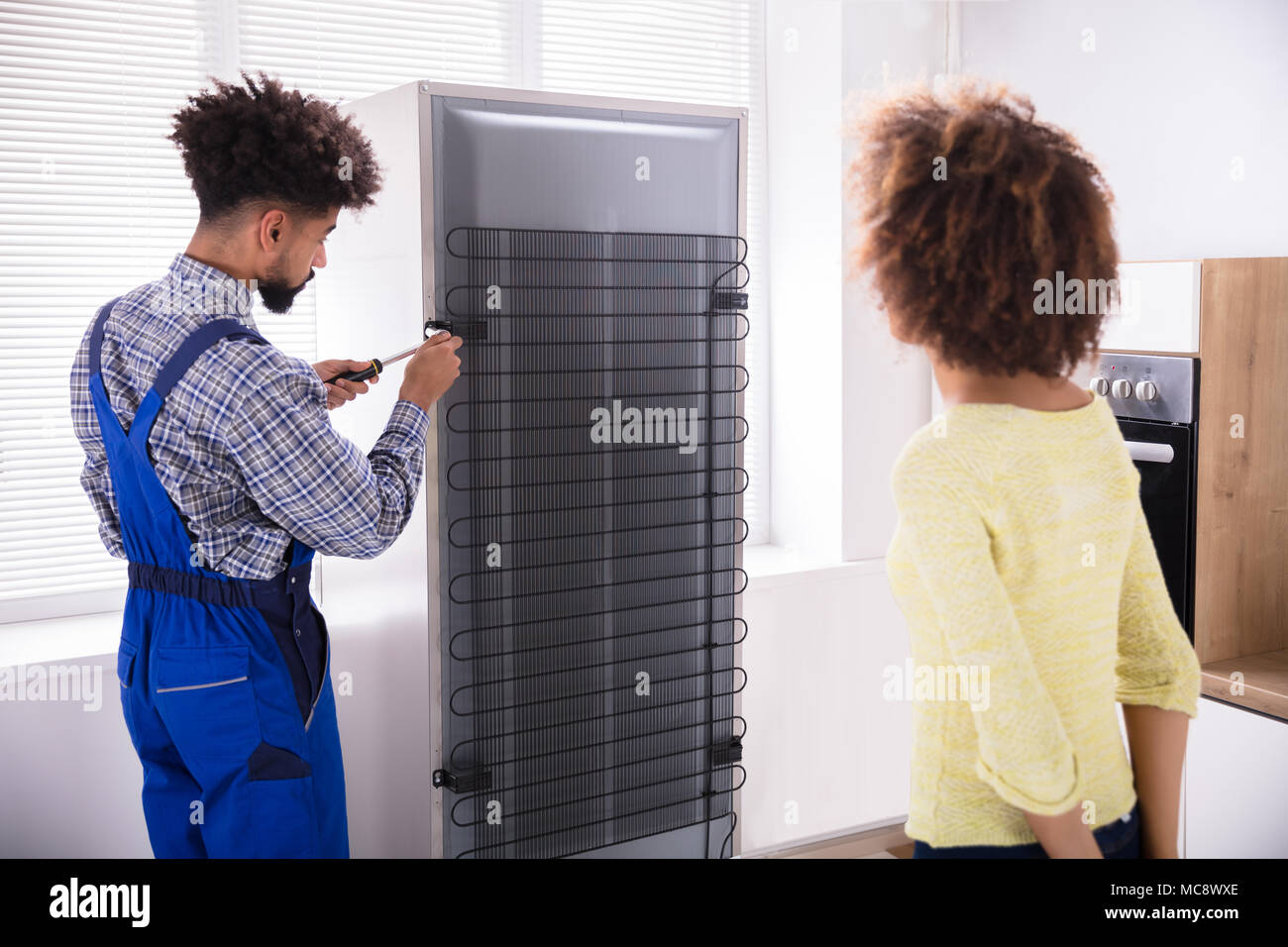 Woman Looking At Technician Repairing Refrigerator With Screwdriver In ...