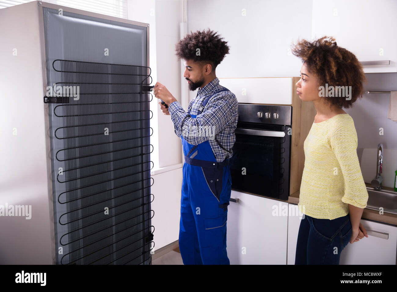 Woman Looking At Technician Repairing Refrigerator With Screwdriver In ...