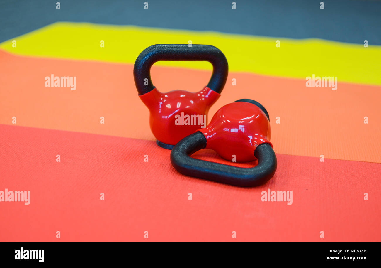 a set of two red kettle bells sitting on colorful exercise mats ...
