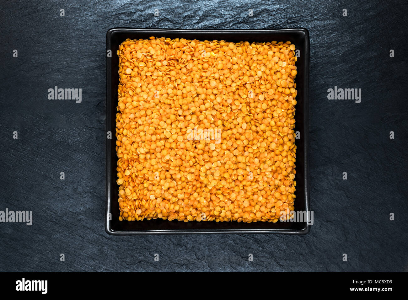 Red lentil grains in black plate on black stone background surface with ...
