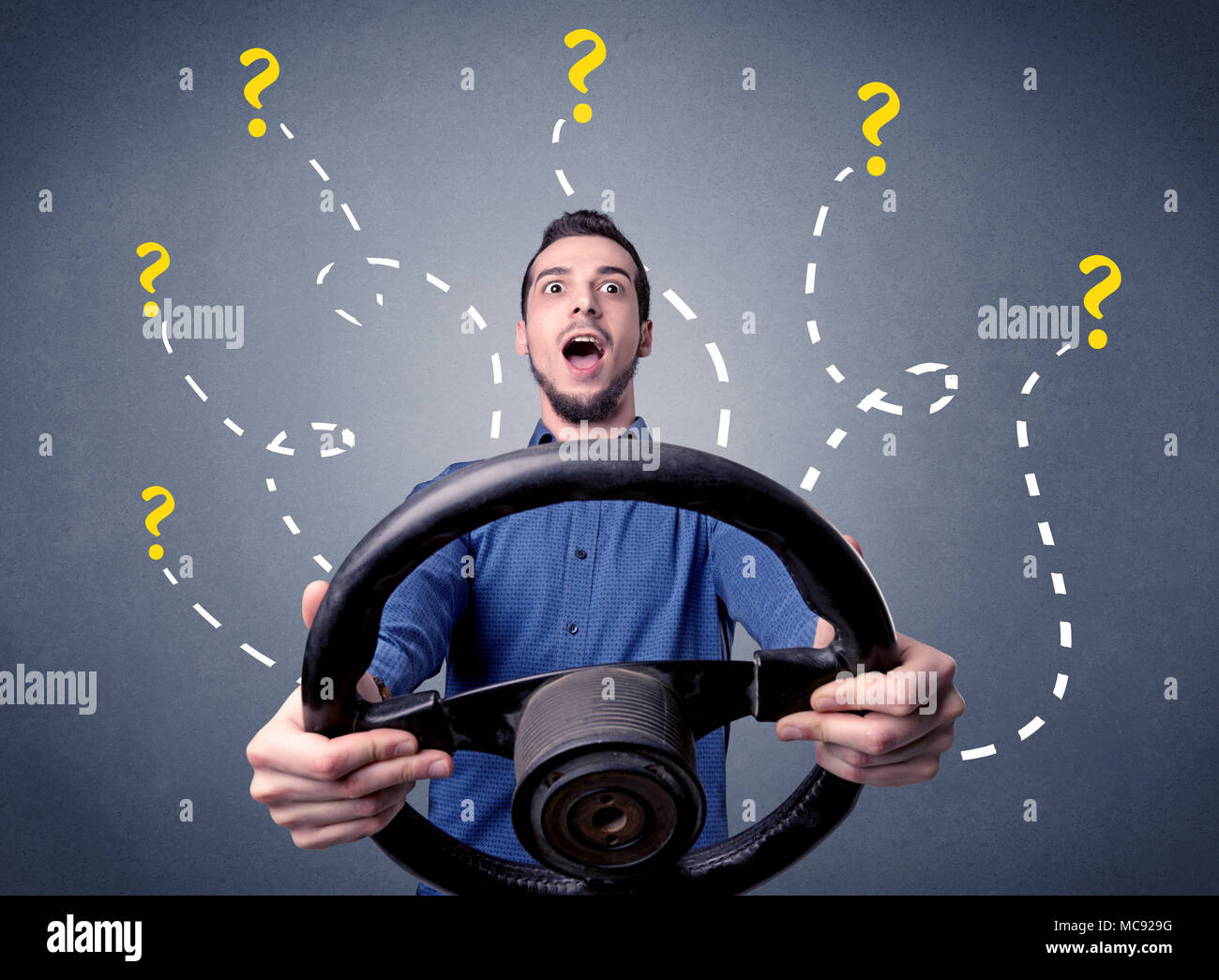 Young man holding black steering wheel with question marks around him ...