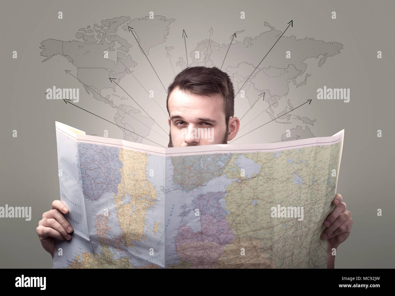 Handsome young man holding a map with world map and arrows behind him ...