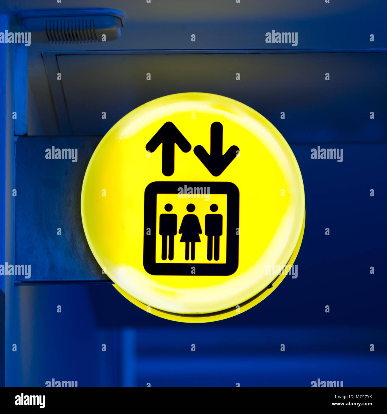 Bright yellow lift or elevator symbol, sign on blue wall background ...