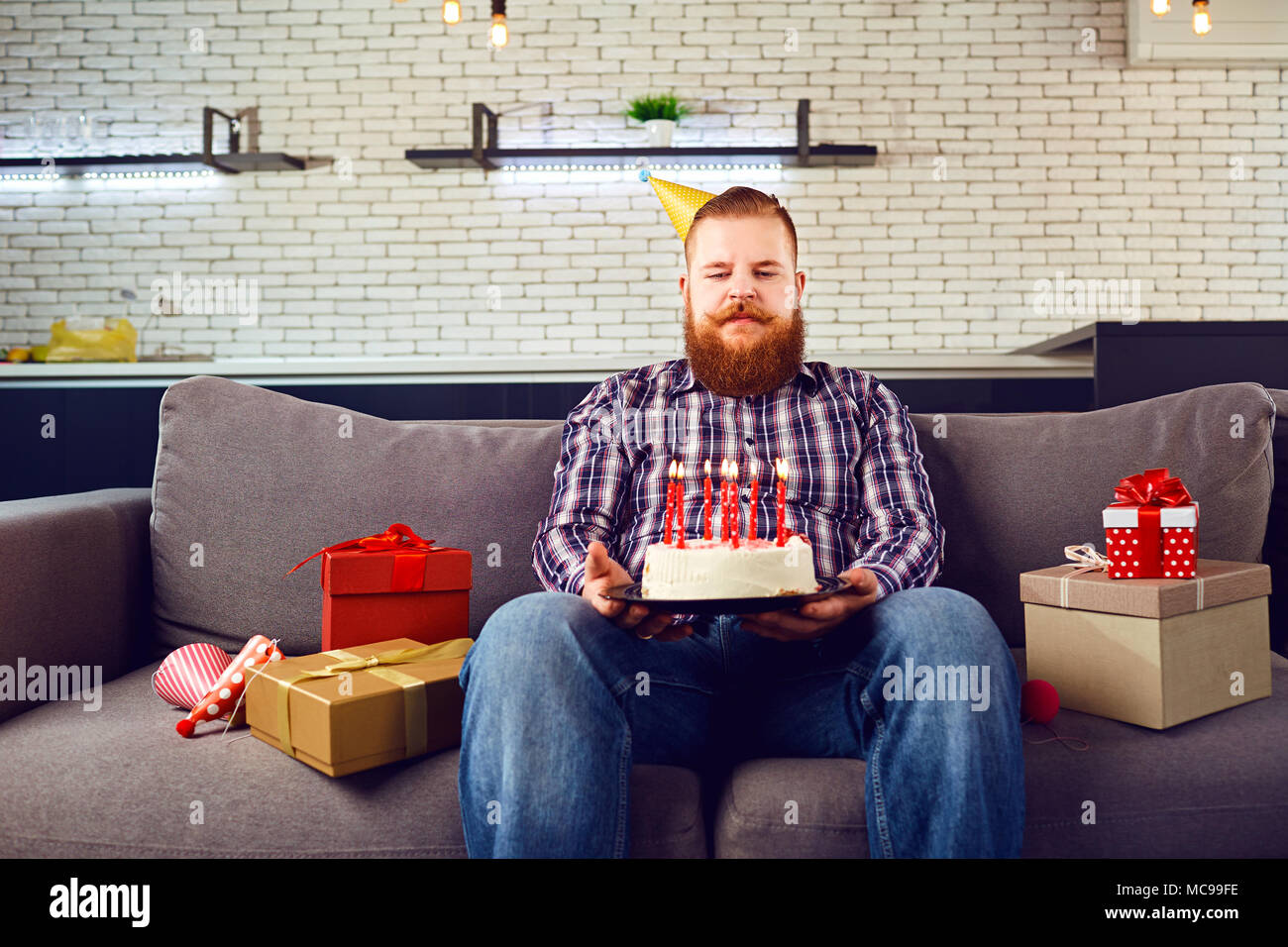 A fat man with a birthday cake sits on the couch in the room Stock ...