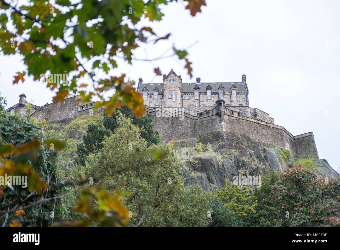Edinburgh Castle behind the tree branches with green and yellow leaves ...
