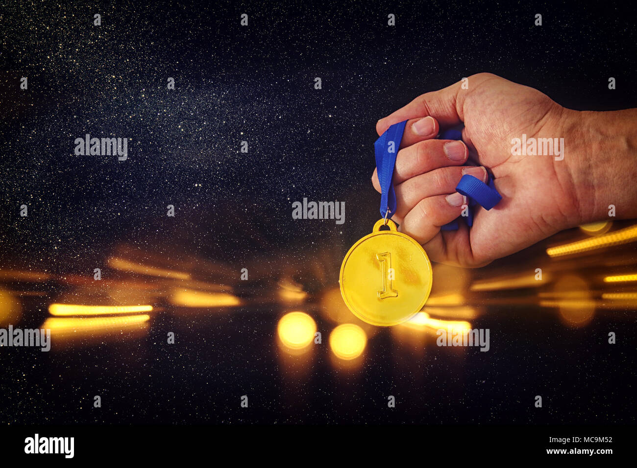 Man hand holding gold medal against black background with glitter ...