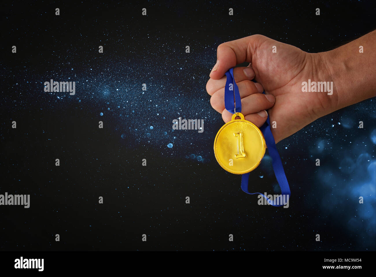 Man hand holding gold medal against black background with glitter ...