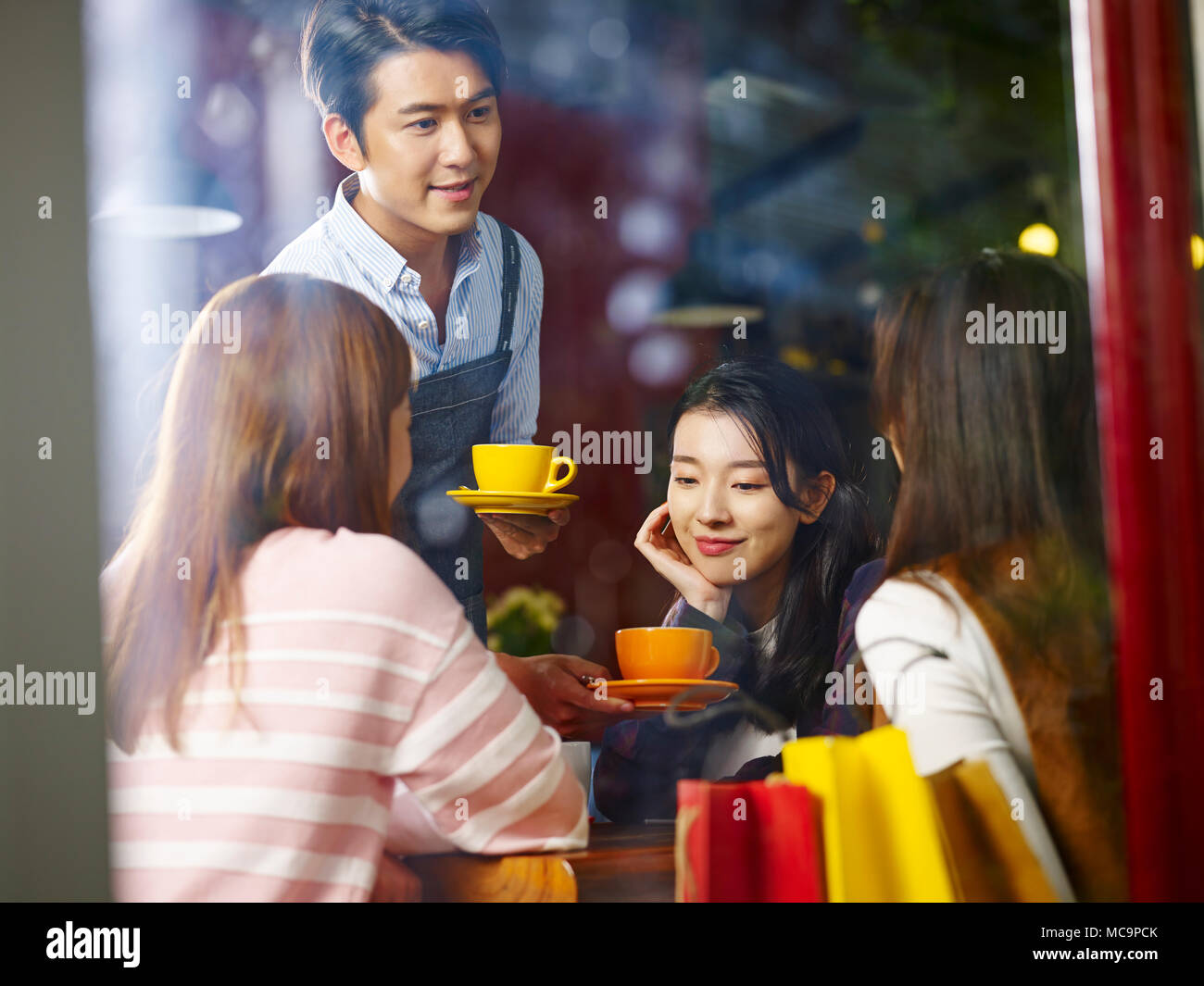 young asian waiter serving female customers in coffee shop, shot ...