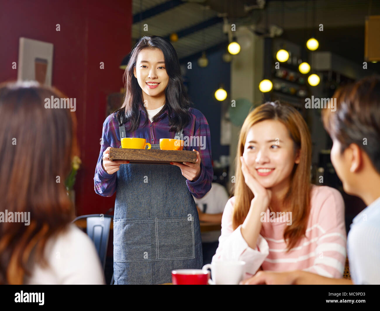 young smiling asian waitress serving customers in coffee shop, focus on ...