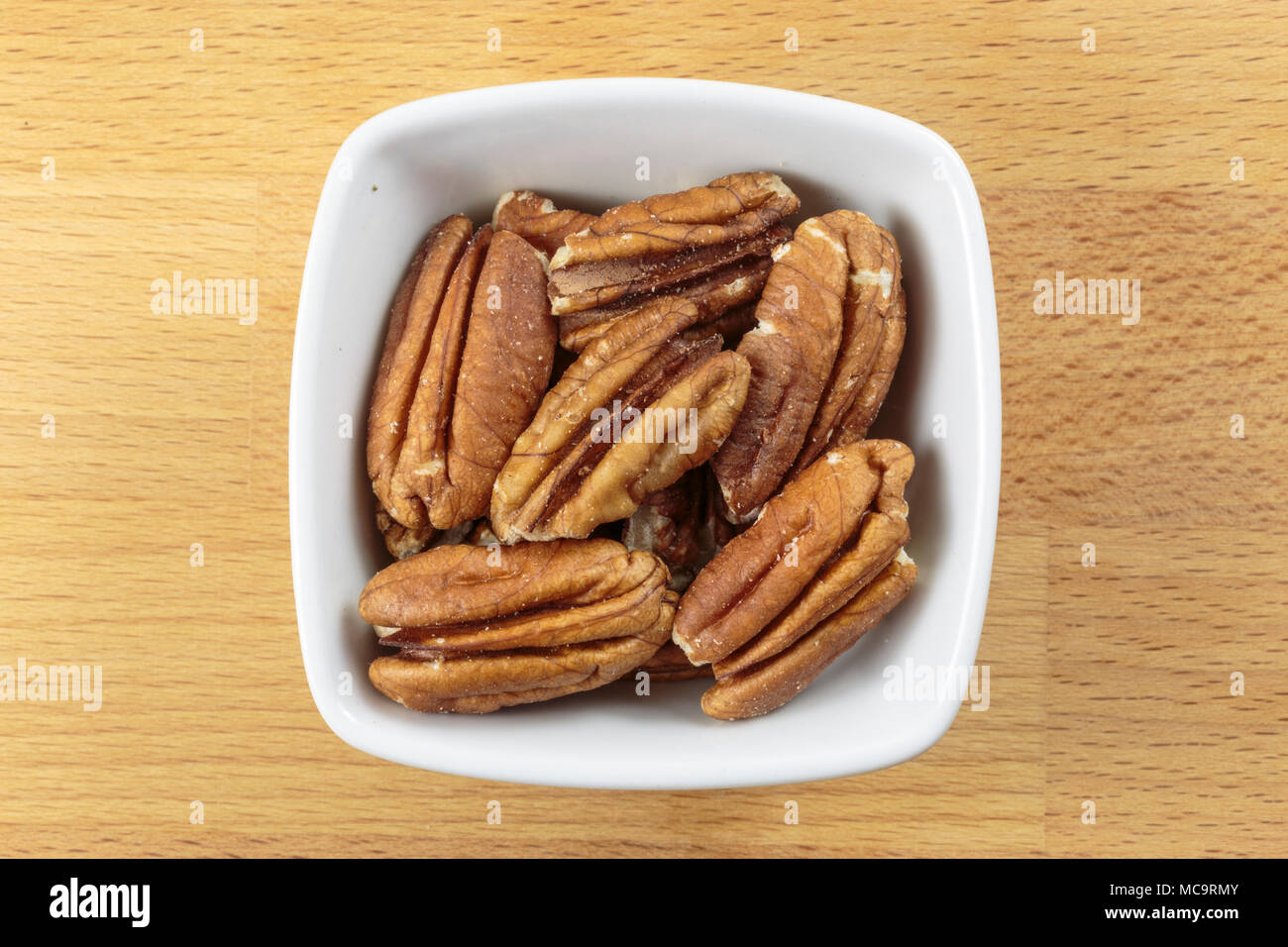 Overhead shot of raw pecan nuts in a white bowl on a wooden chopping ...