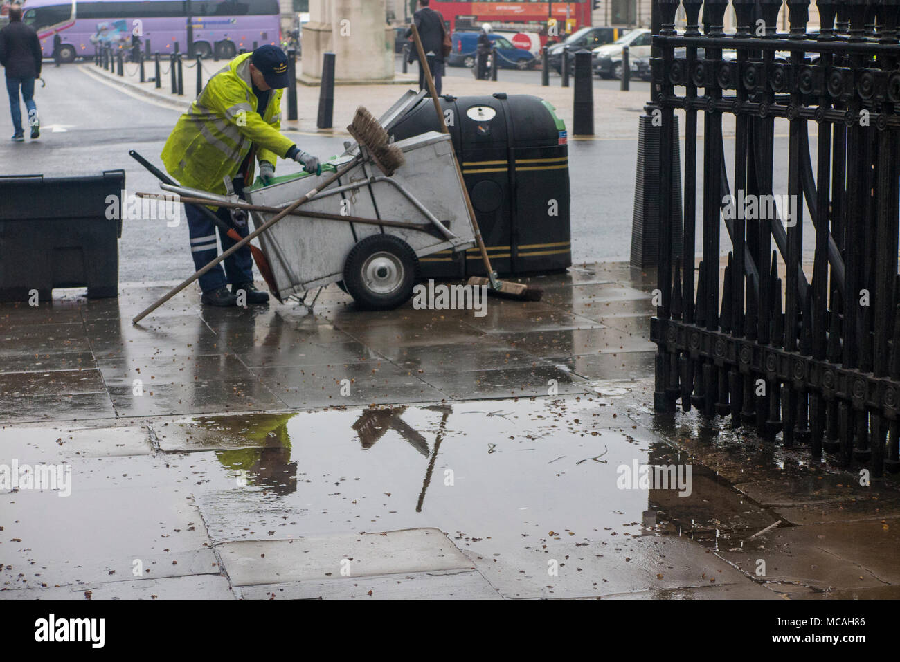 A street sweeper emptying a bin is reflected in a puddle on a rainy ...