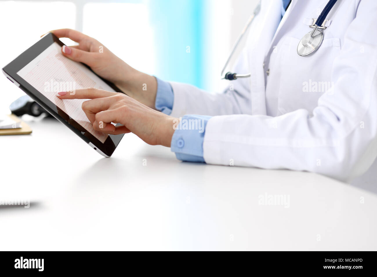 Woman doctor using tablet computer while sitting at the desk in ...