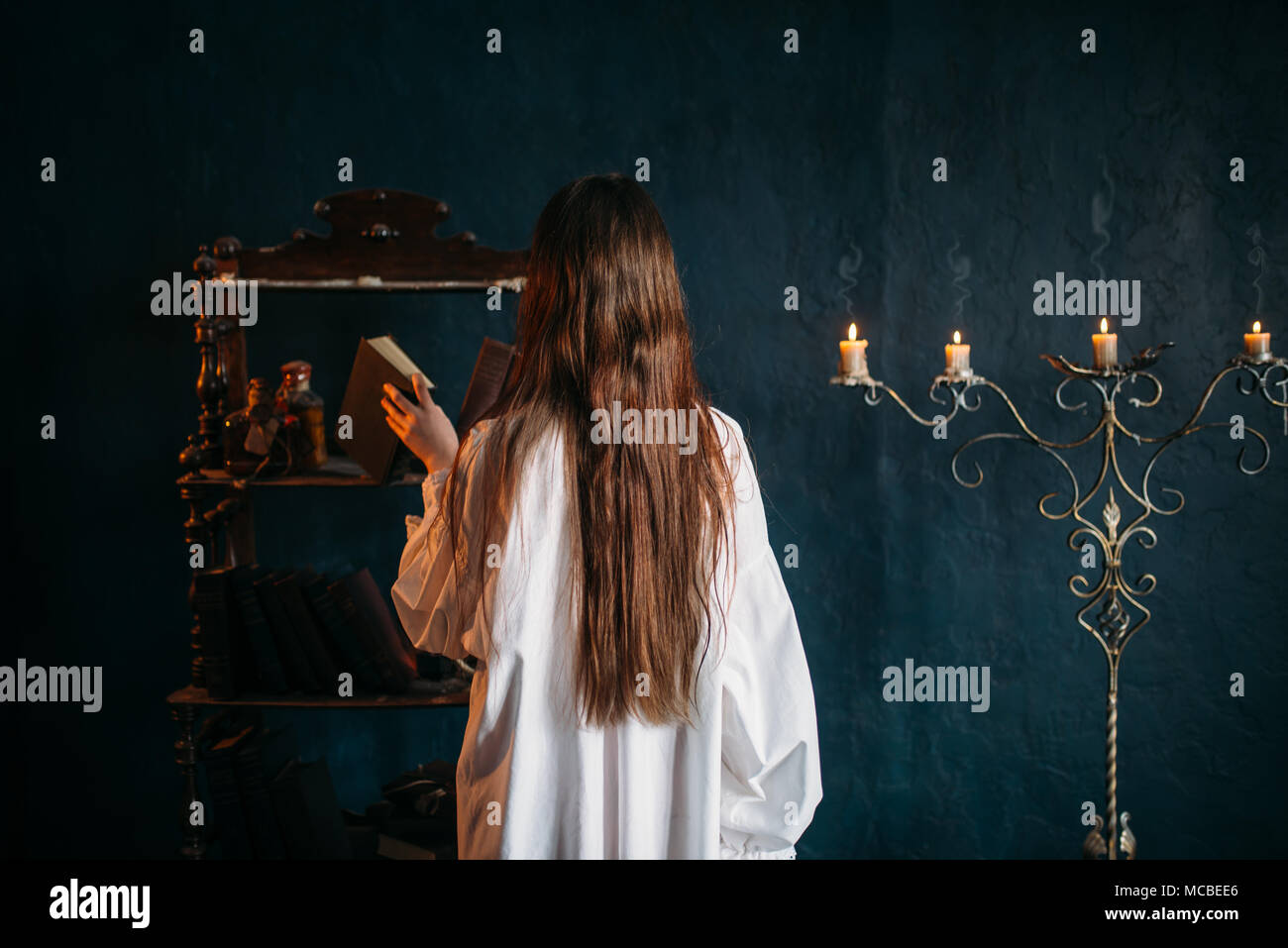 Female puts old spellbook on shelf, back view Stock Photo - Alamy