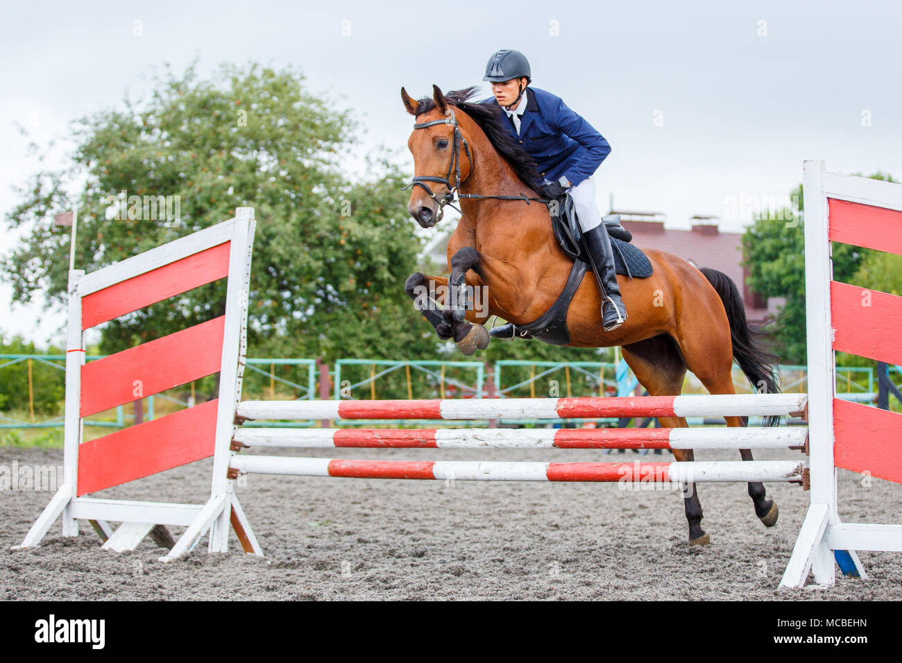 Young rider man jumping on horse over obstacle on show jumping ...