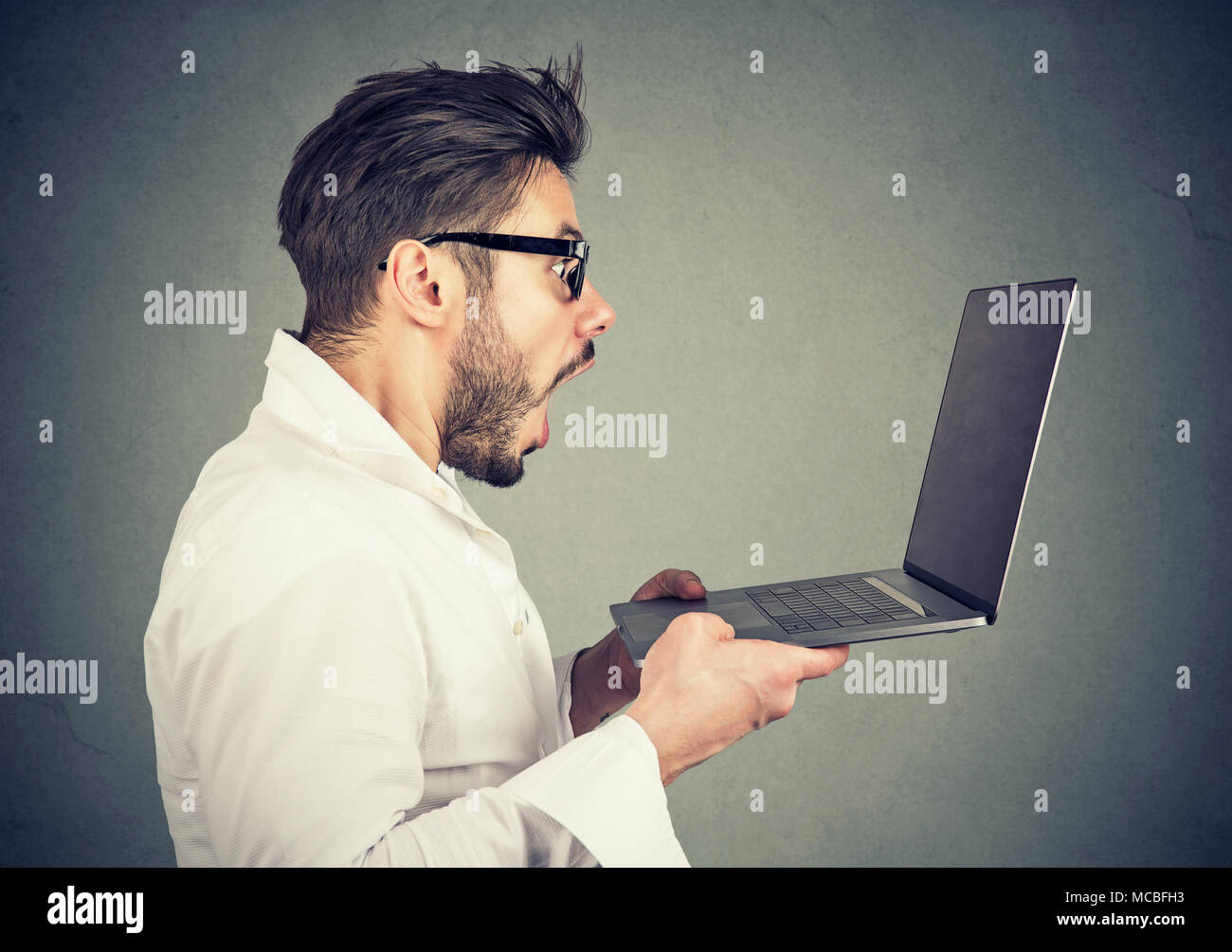 Surprised young man with laptop computer Stock Photo - Alamy