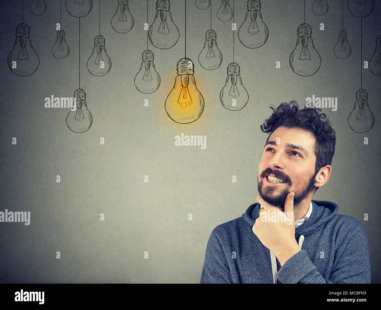 Portrait of a thinking man smiling looking up at light idea bulb above ...