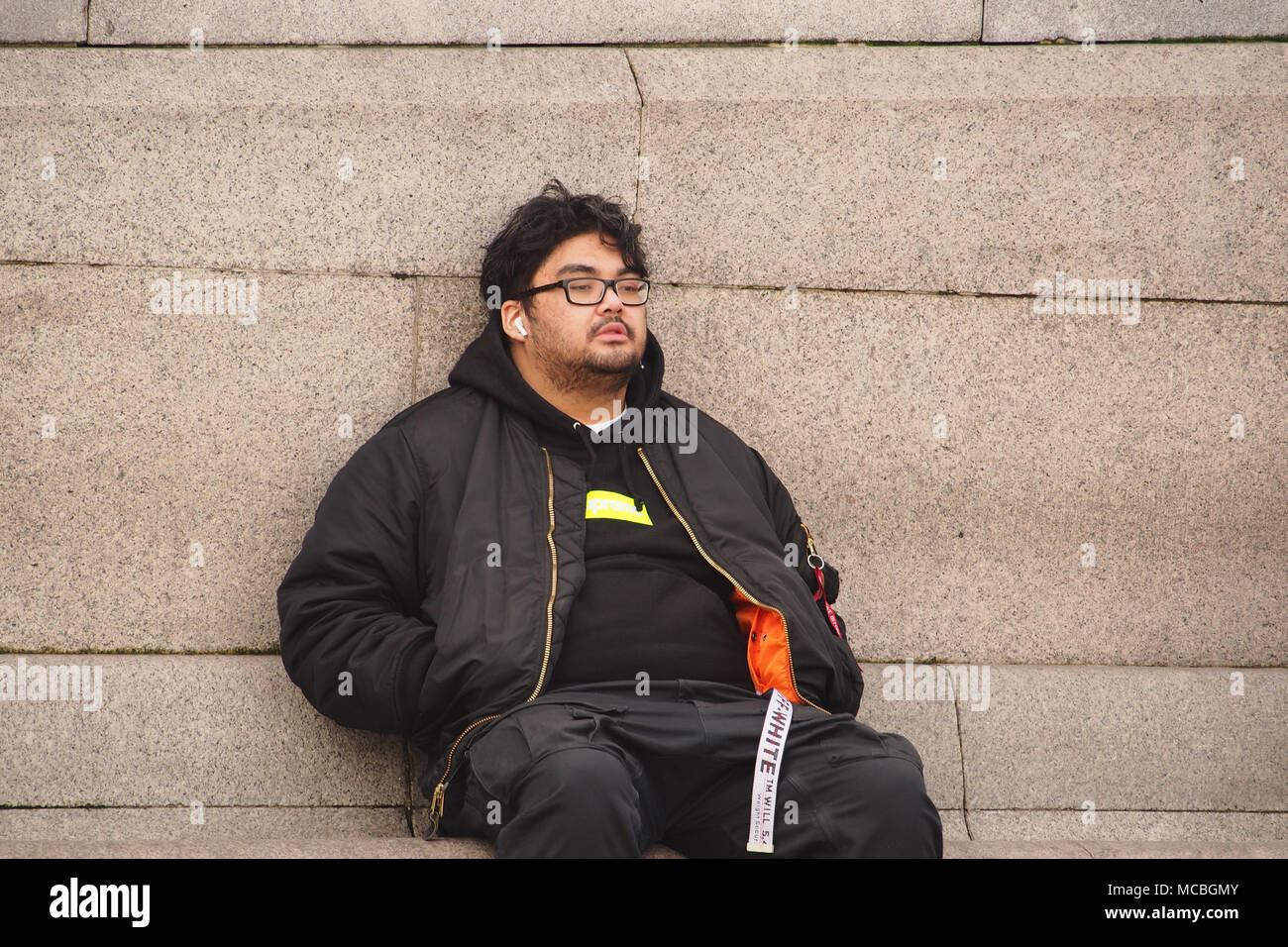 A young man sitting in a slouched mode in Trafalgar Square on a stone ...