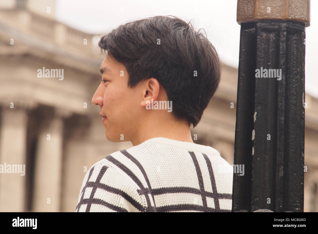 A young man sitting by a lamp post in Trafalgar Square, London watching ...