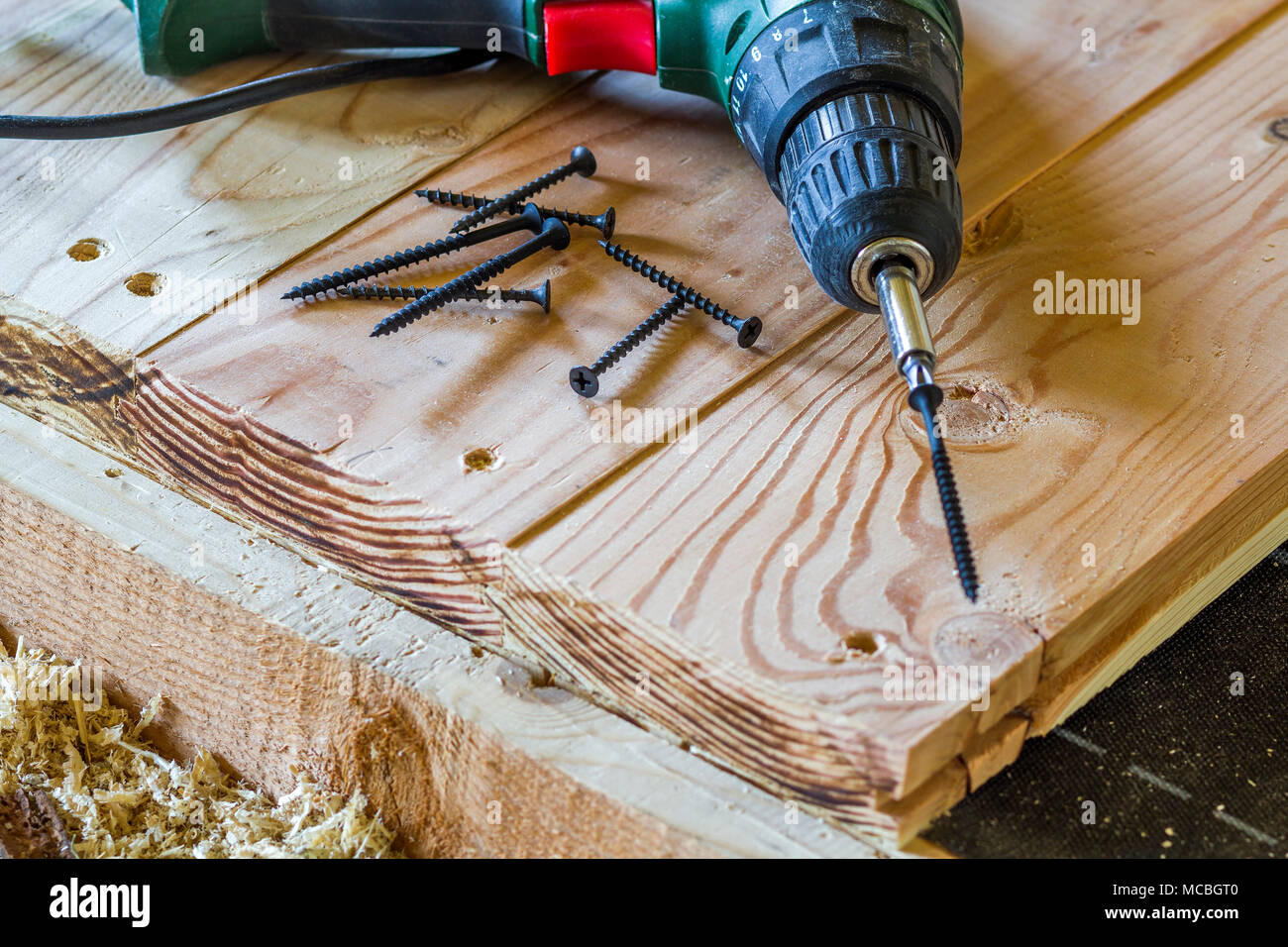 Close up of electric screwdriver with some screws laying on old rough ...