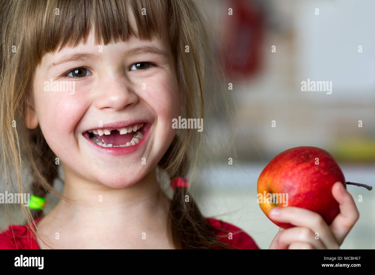 A cute little curly toothless girl smiles and holds a red apple ...