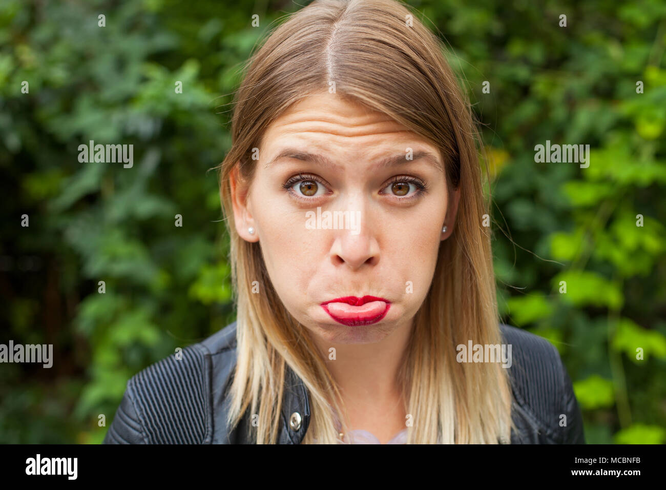 Young woman making a grimace outdoor, green background. Sad - grumpy ...