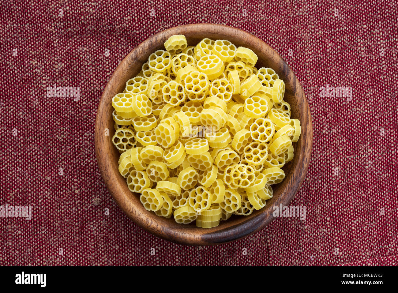 Macaroni ruote pasta in a wooden bowl on a red brown rustic texture ...