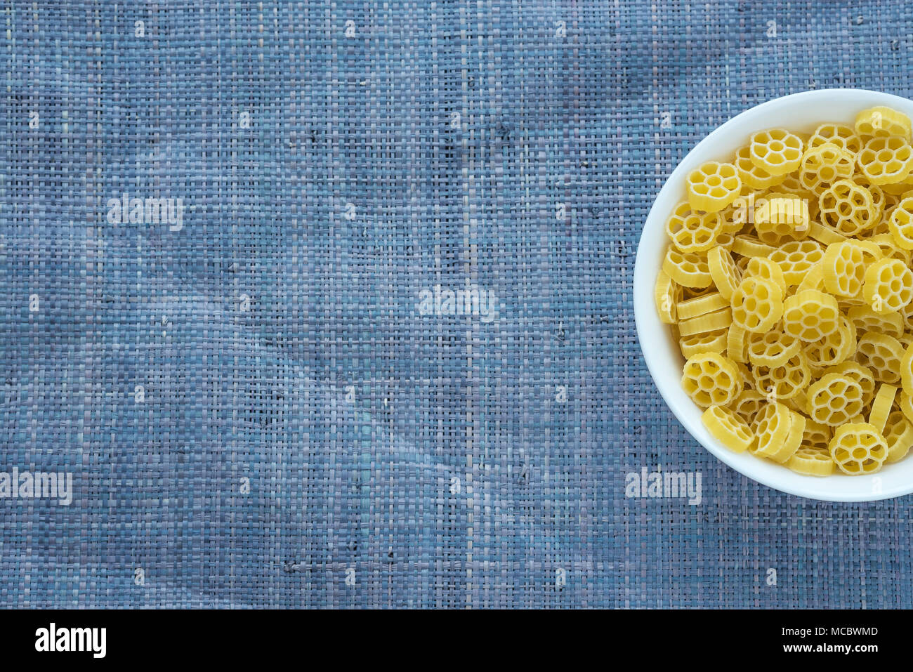 Macaroni ruote pasta in a white bowl on a blue knitted textured ...