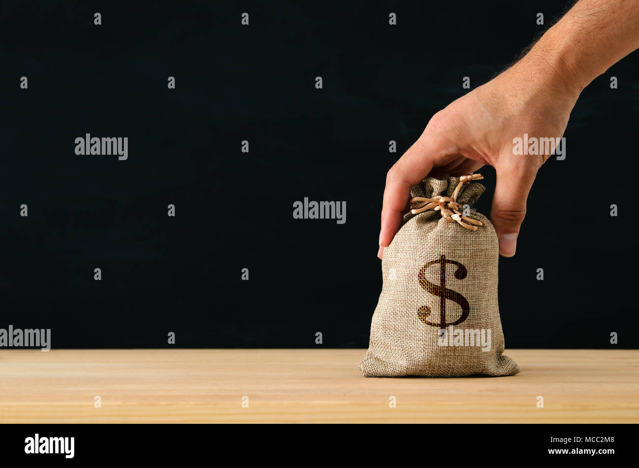 Male hand holding a sack of money over wooden desk Stock Photo - Alamy