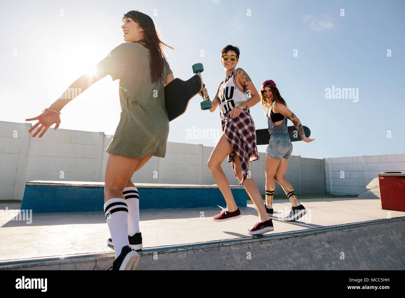 Three female friends running and jumping over skate park ramp. Women ...