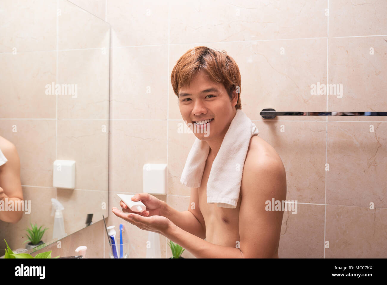 Young handsome asian man applying cream onto face in bathroom Stock ...