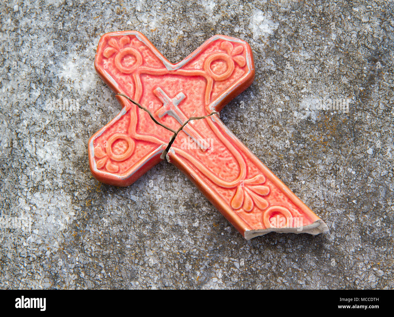 Broken orange ceramic cross on gray stone background Stock Photo - Alamy