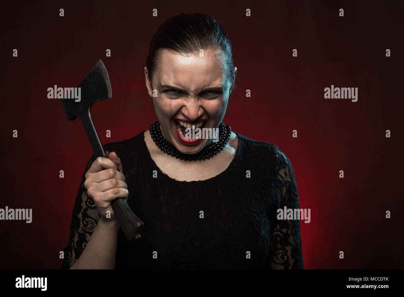 angry woman with smeared cosmetics and hatchet on dark red background ...