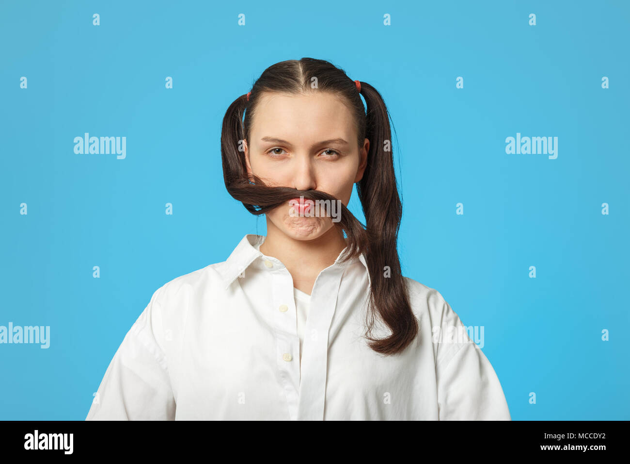 pretty young woman on blue background making mustache with her hair ...