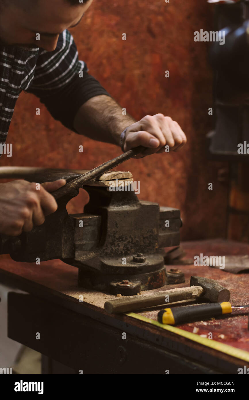 Man works in carpentry workshop. He files excess wood with an ax Stock ...