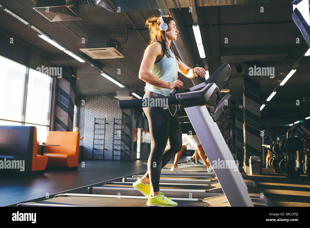 Beautiful young woman with long hair trains in the gym on a treadmill ...