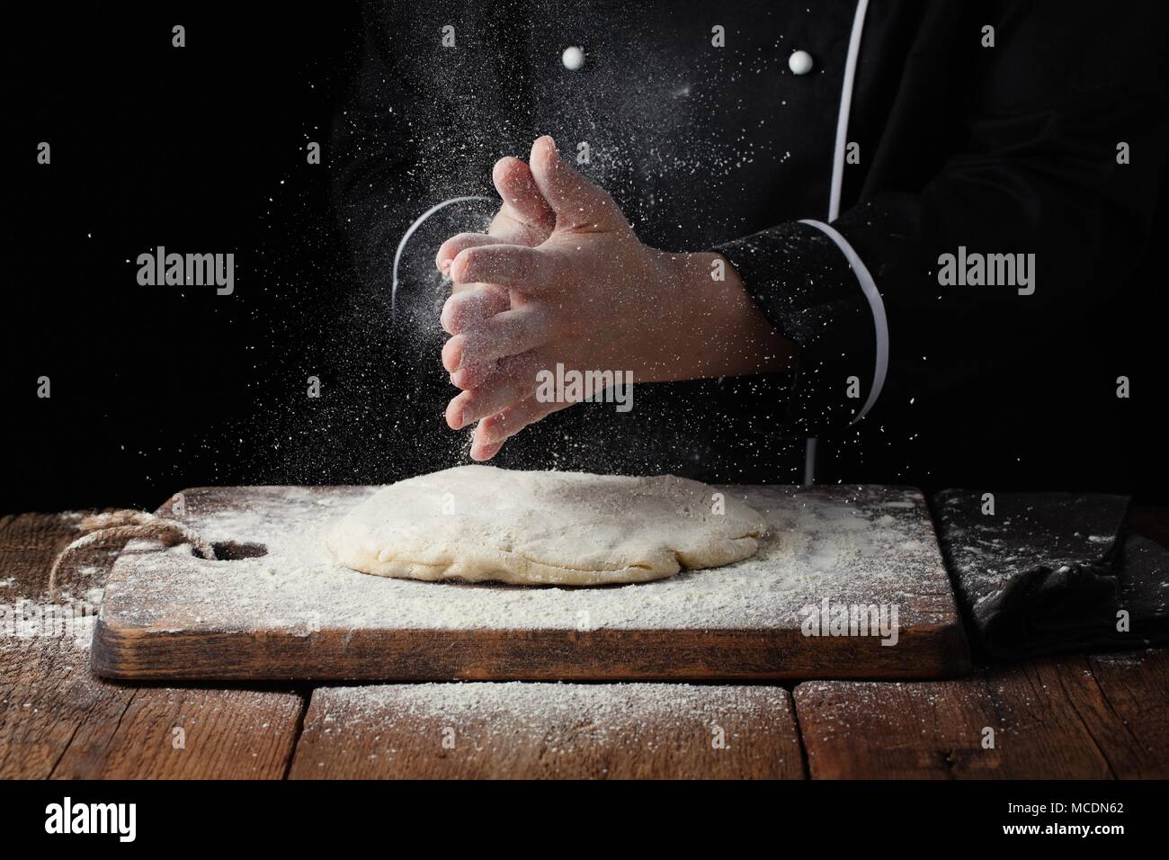 Woman chef hand clap with splash of white flour on a black background ...