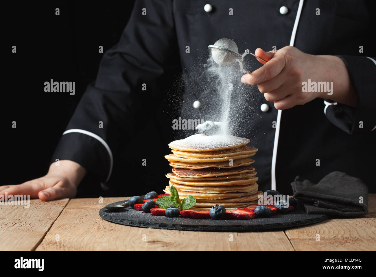 Serving pancakes with powdered sugar and berries. Chef woman hand ...