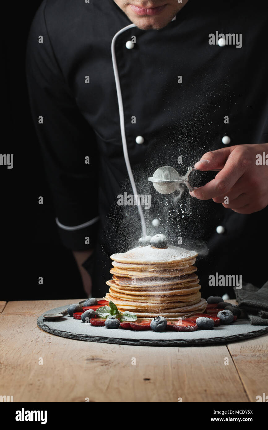 Serving pancakes with powdered sugar and berries. Chef man hand ...