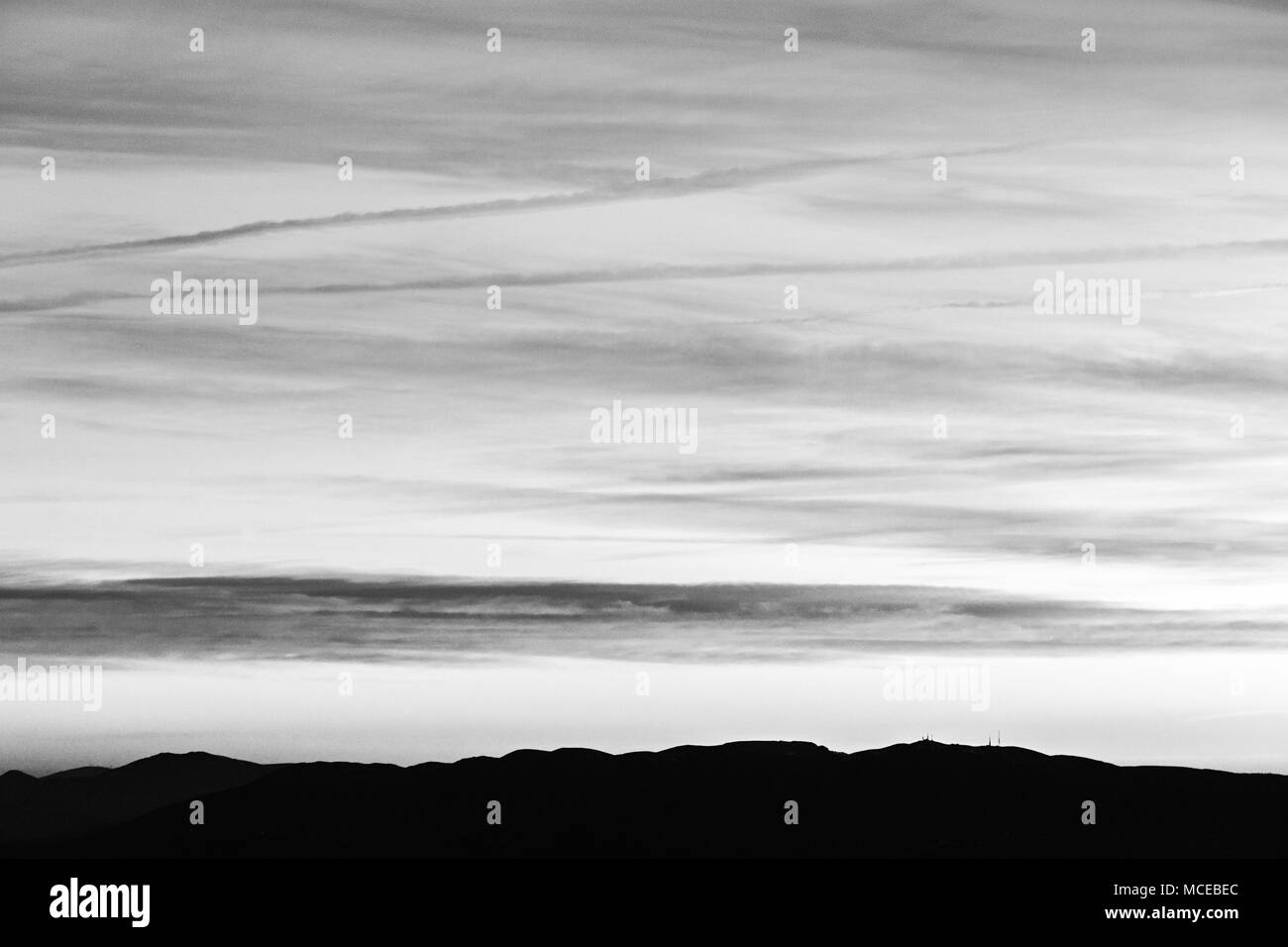 Sunset over distant mountains, with deep sky full of white clouds and ...