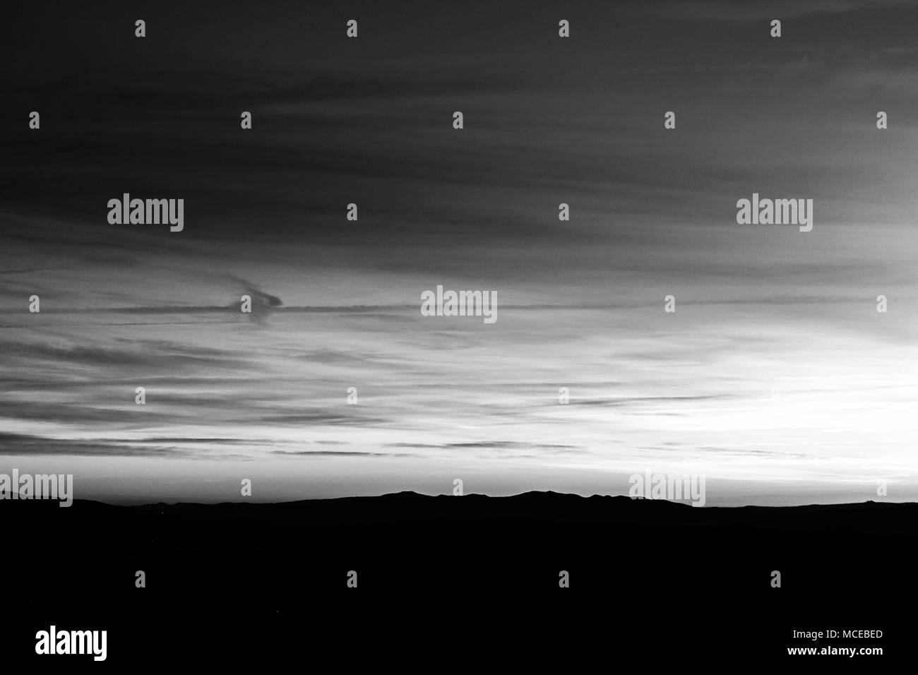 Sunset over distant mountains, with deep sky full of white clouds and ...