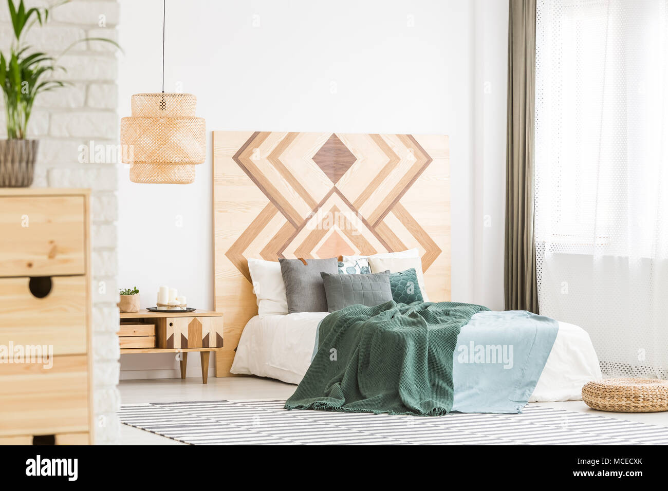 Green bedding on bed against wooden geometric board in natural bedroom ...
