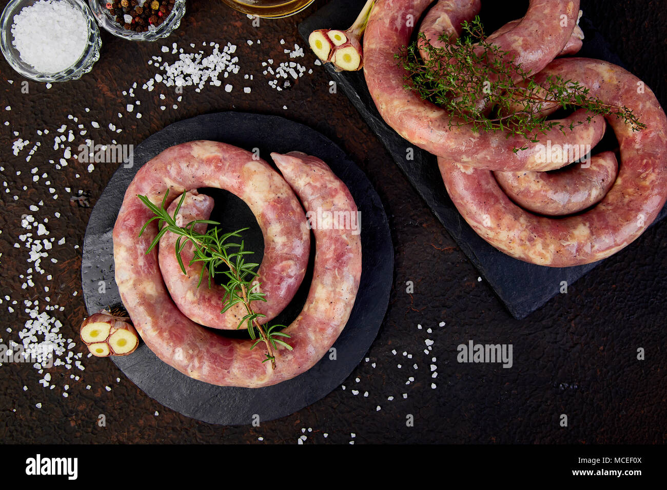 Raw spiral pork sausages with rosemary, salt and peper on black slate ...