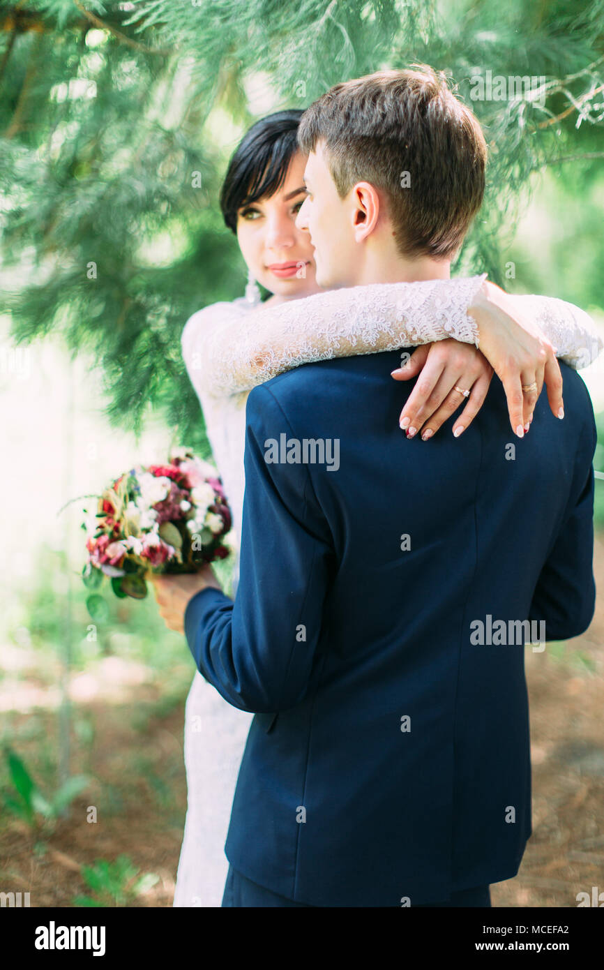 The hugging newlyweds in the forest. Back view of the groom Stock Photo ...
