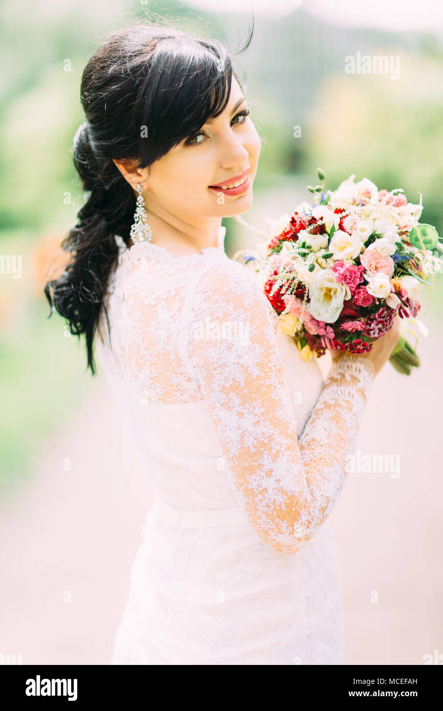 The lovely outdoor portrait of the smiling bride holding the colourful ...