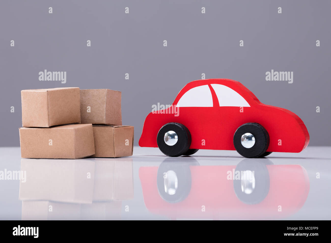 Red Car And Cardboard Boxes On White Desk Against Grey Background Stock ...