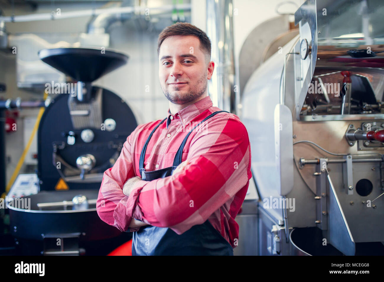 Image of young man in apron on background of industrial coffee grinder ...