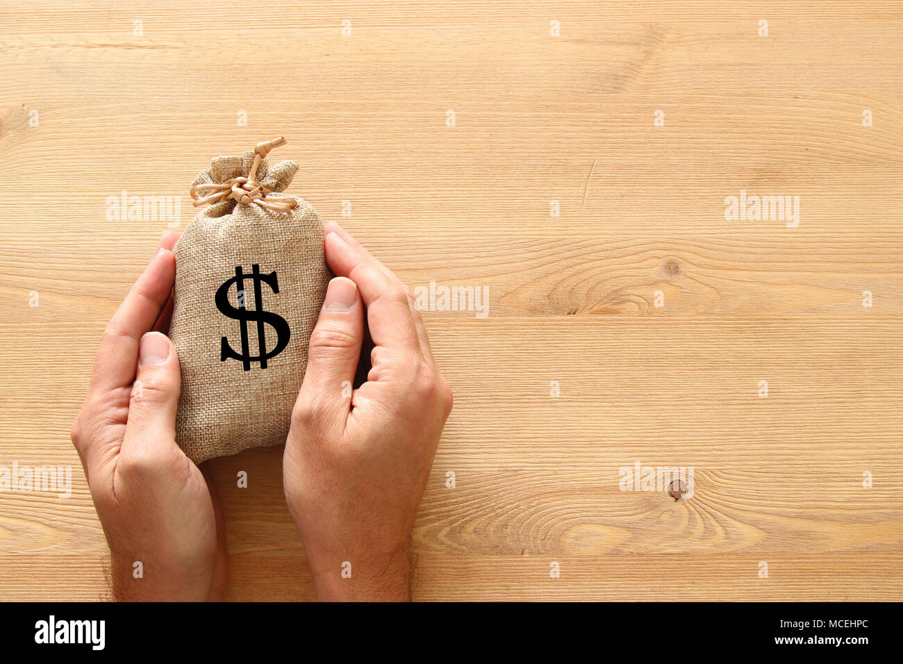 Male hand holding a sack of money over wooden desk Stock Photo - Alamy