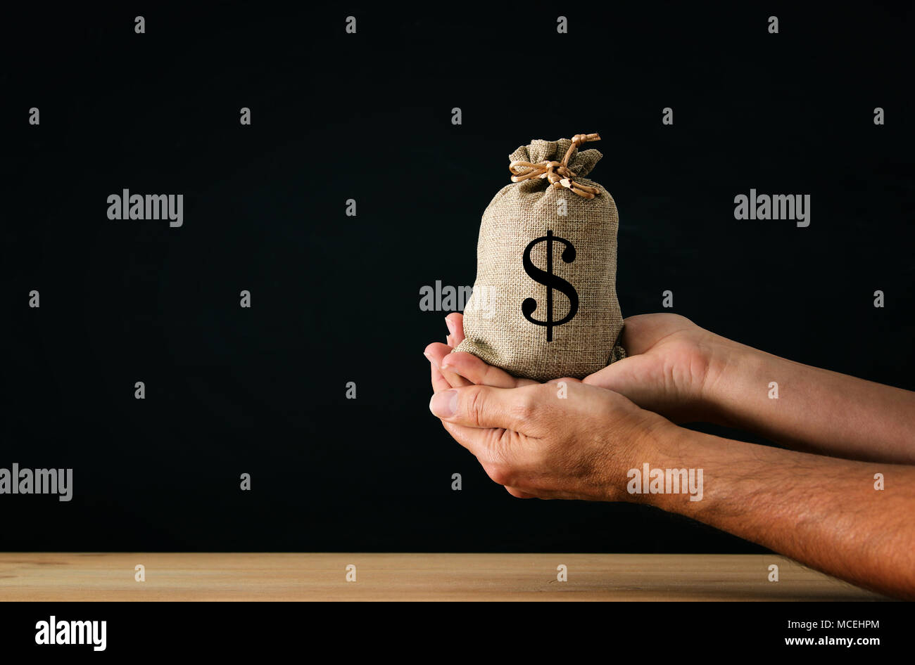 Male hand holding a sack of money over wooden desk Stock Photo - Alamy
