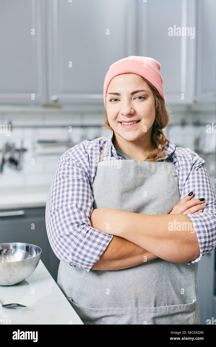 Portrait of young Caucasian female cook in apron standing in kitchen ...